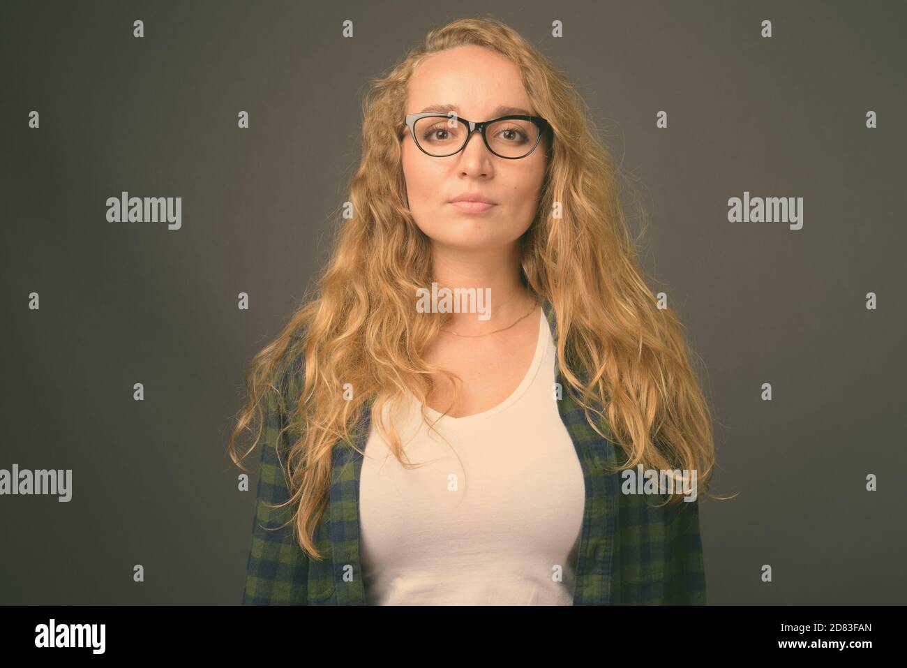 Young beautiful woman with long wavy blond hair against gray background ...