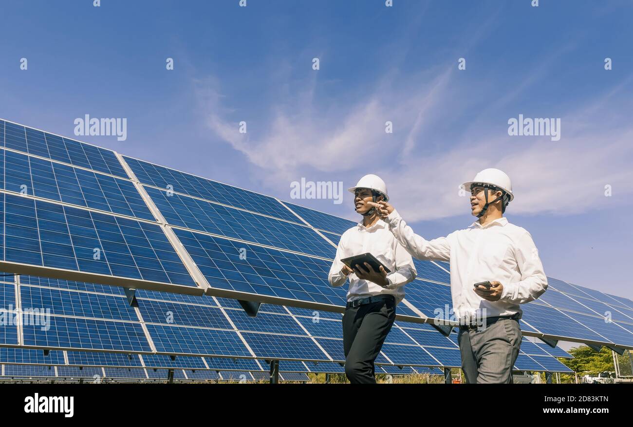 The solar farm(solar panel) with two engineers walk to check the ...