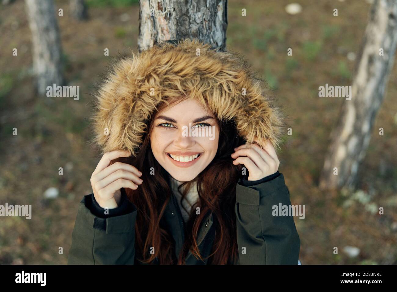 Woman with a hood on her head smiling leaning against a tree on nature ...