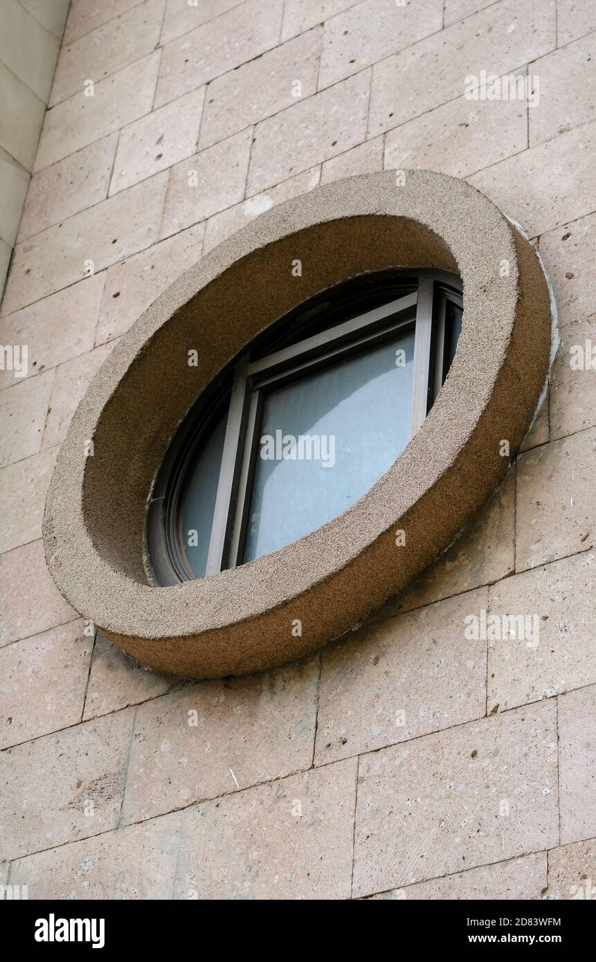 Round window with square window frame inside on facade of stone wall ...