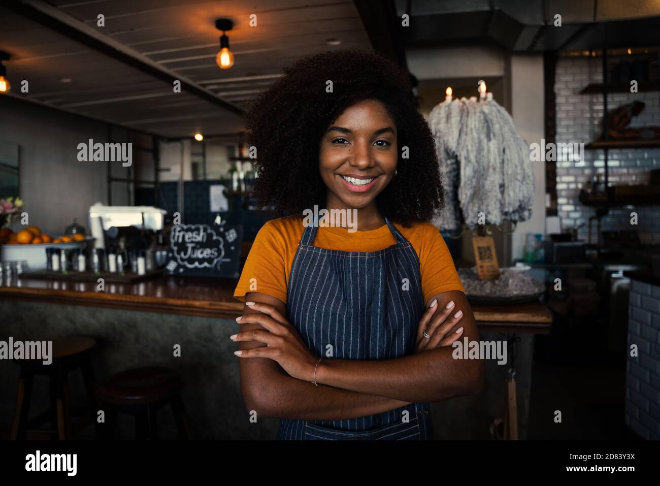 Beautiful smiling waitress wearing apron standing cross-armed in trendy ...