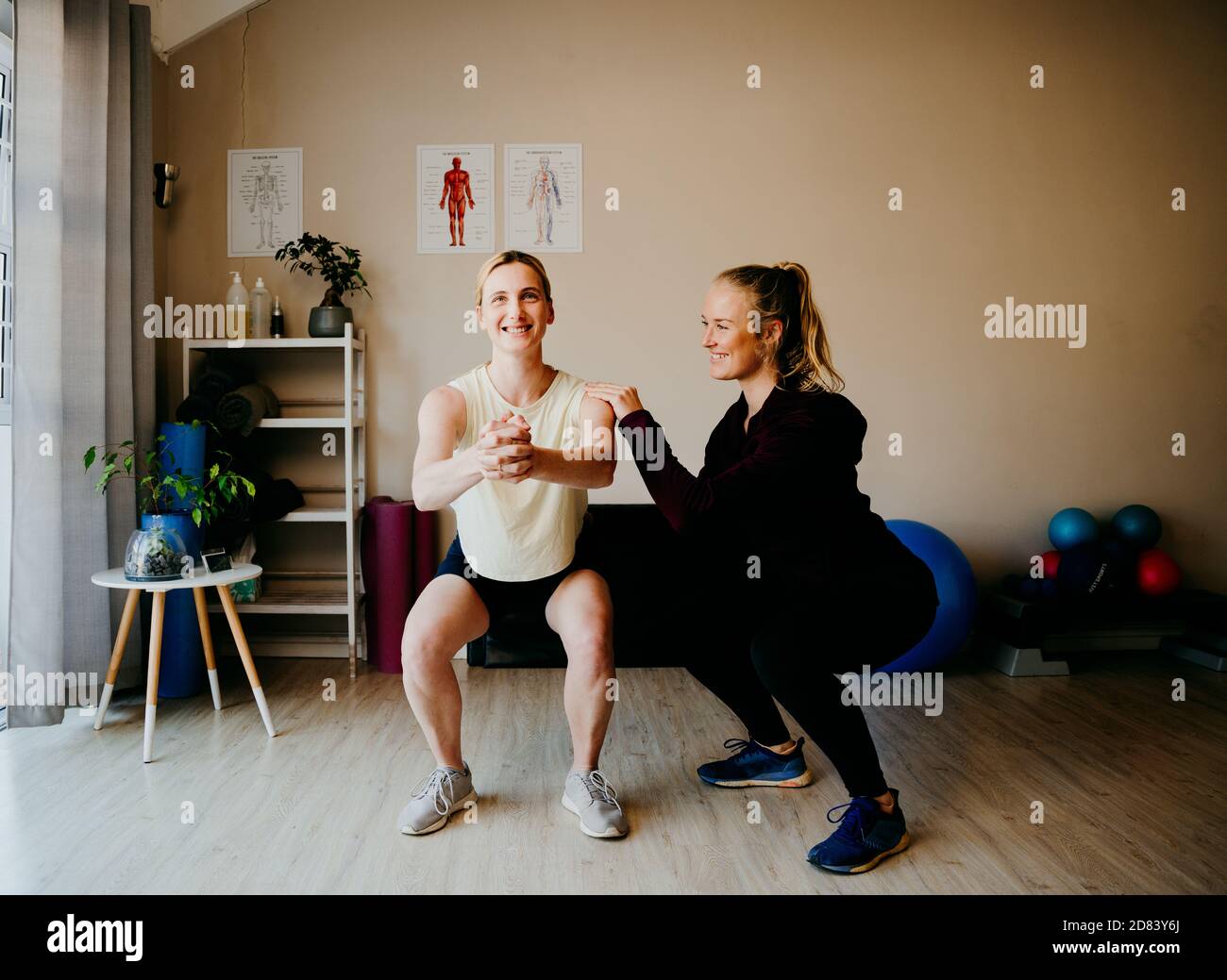 female patient holding squat position in exercise studio while physio ...