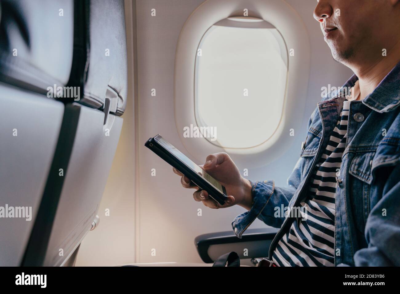 20s young adult male tourist holding a cellphone inside aircraft cabin ...