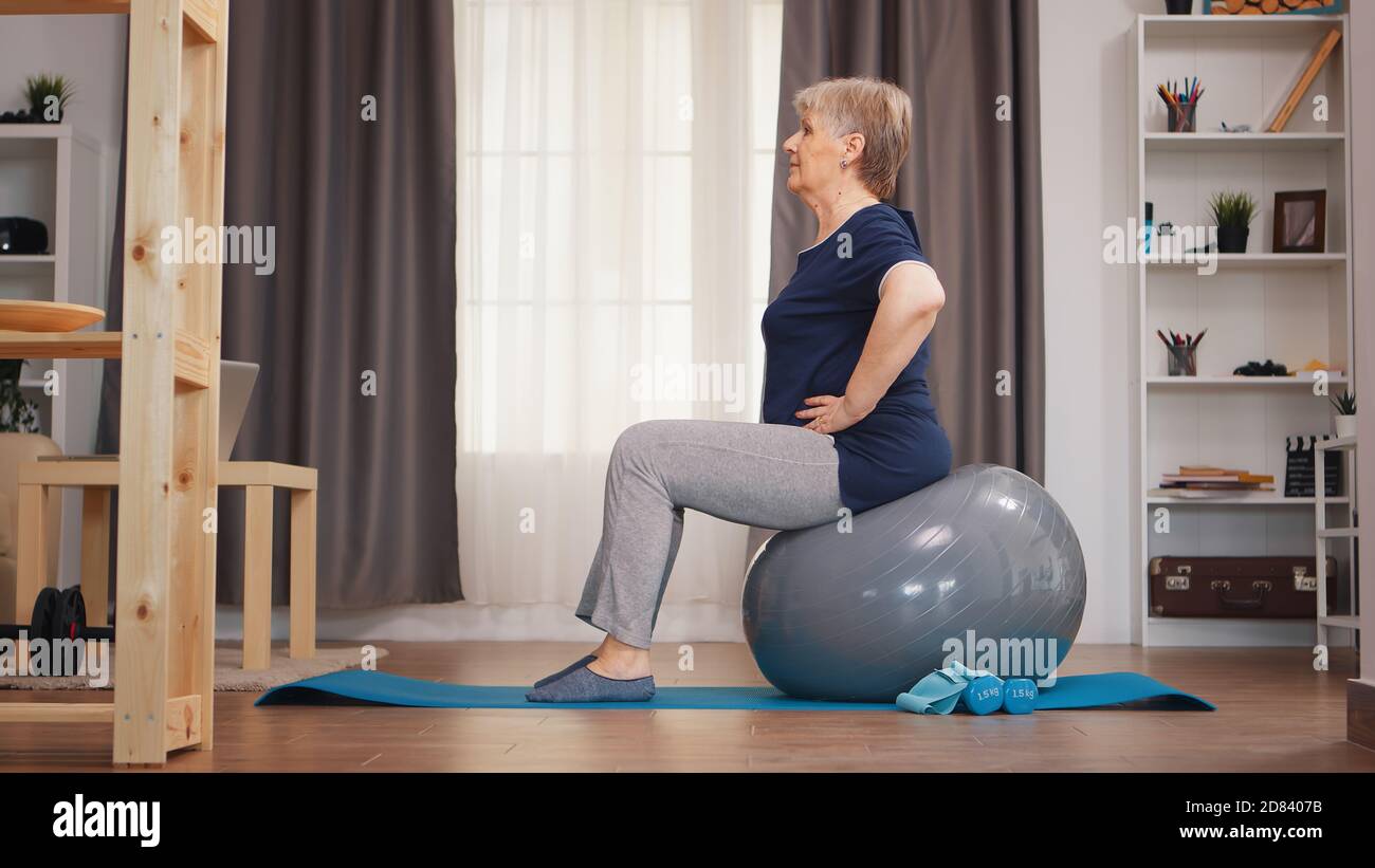 Old woman workout on training ball in living room. Old person training ...
