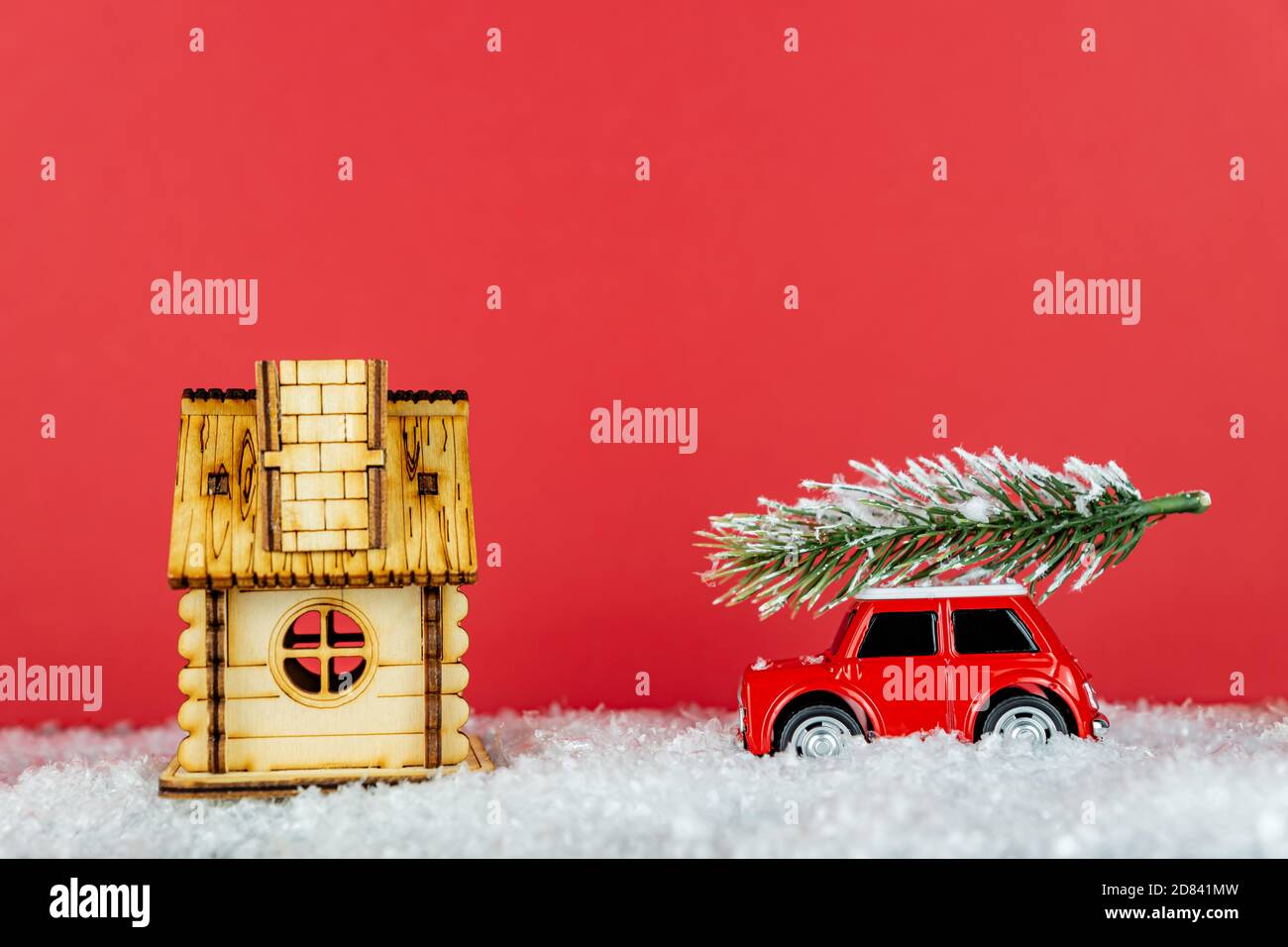 Small red toy car carrying spruse tree on a snowe road next to wooden ...