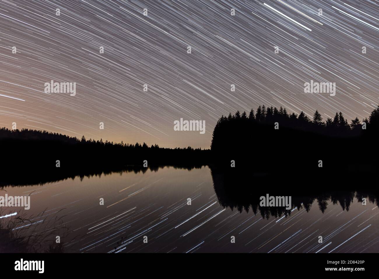 Star trails in a starry night in front of a reservoir with reflections ...