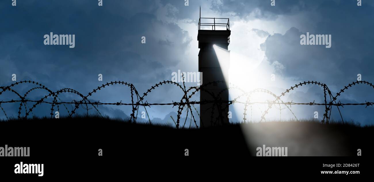 a watchtower with spotlight behind barbed wire as a symbol of division ...