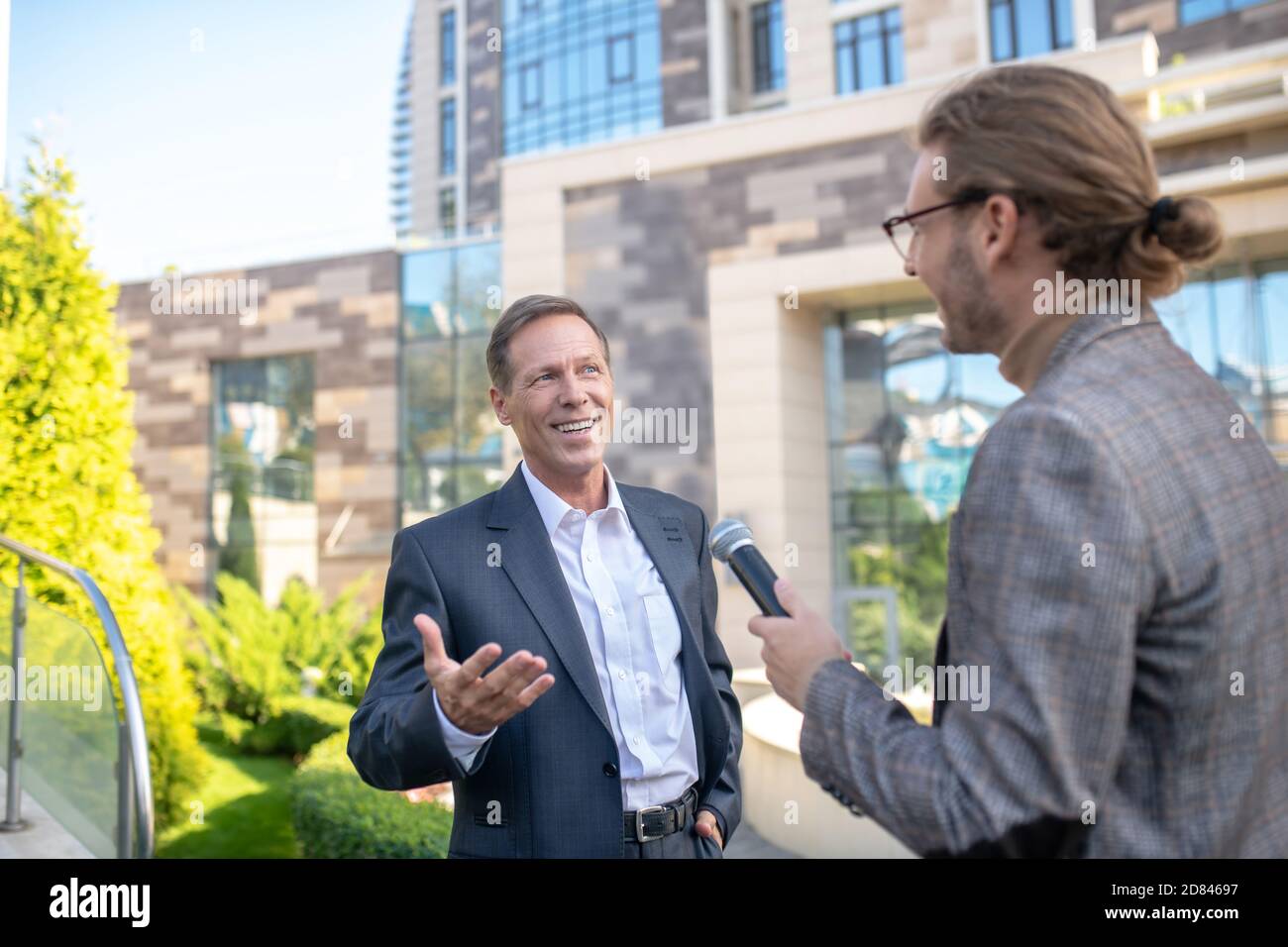 Smiling male answering questions of long-haired male journalist Stock Photo - Alamy