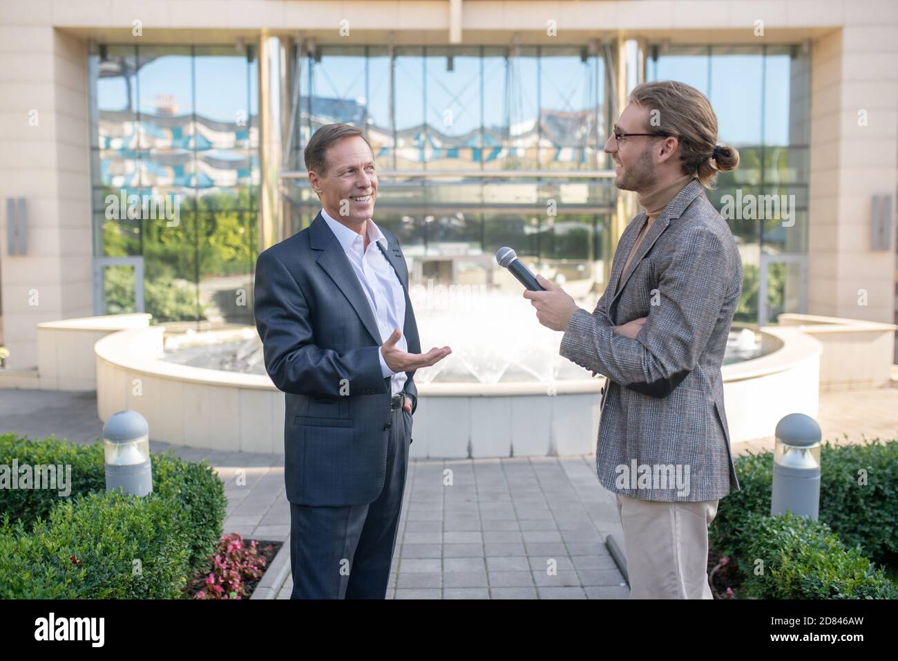 Long-haired male journalist having interview with smiling mature male ...