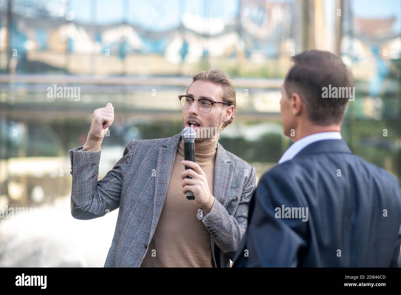 Male journalist speaking into microphone, interviewing mature male ...