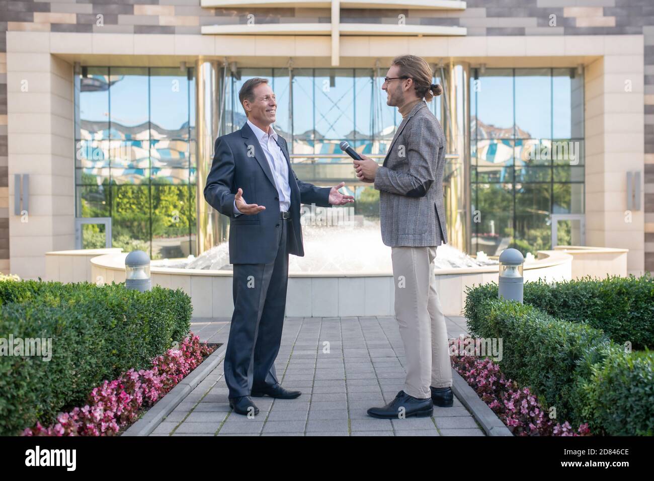 Fair-haired male journalist interviewing mature male in suit outside ...