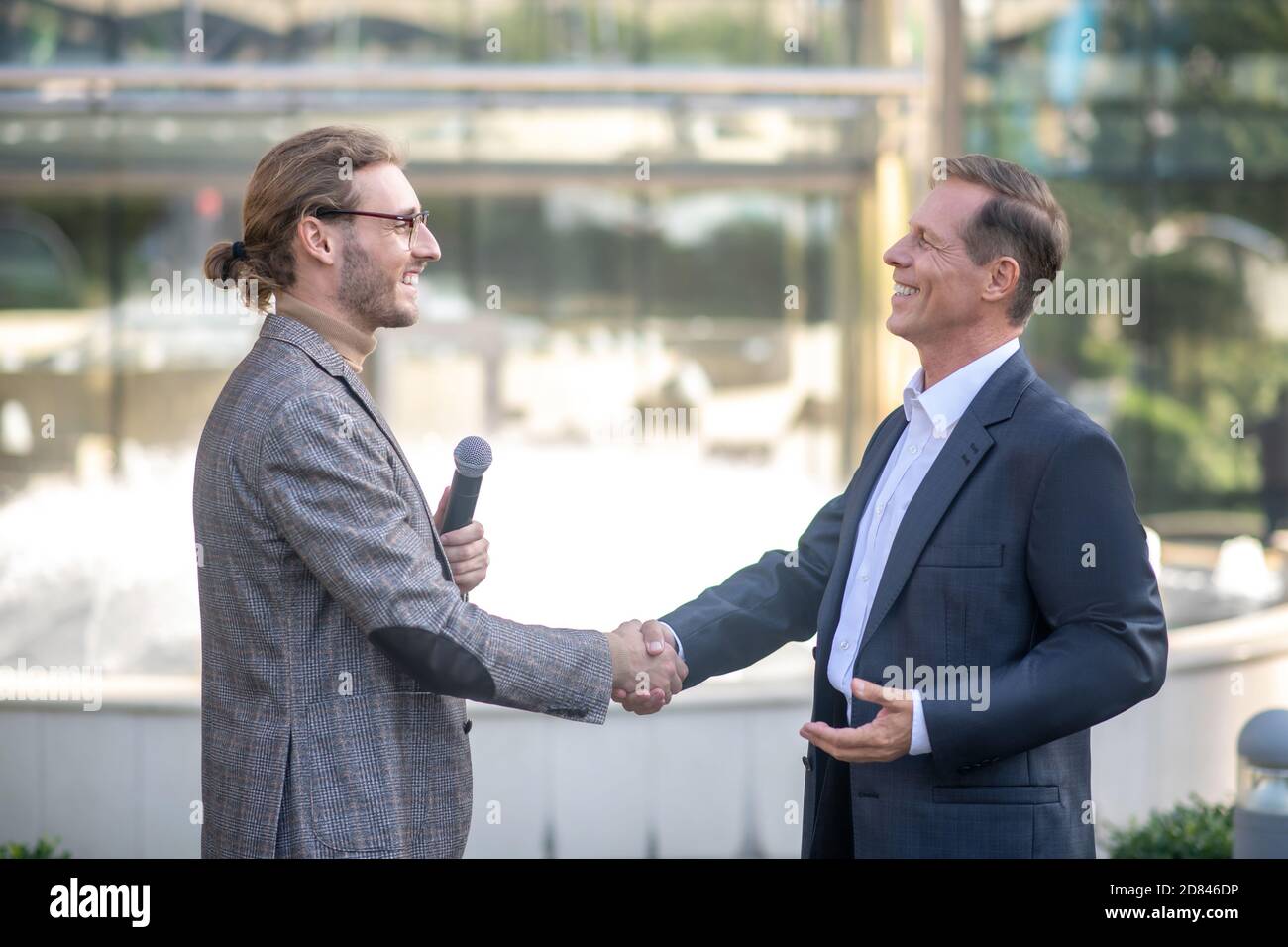 Male interviewee and fair-haired male journalist shaking hands outside ...