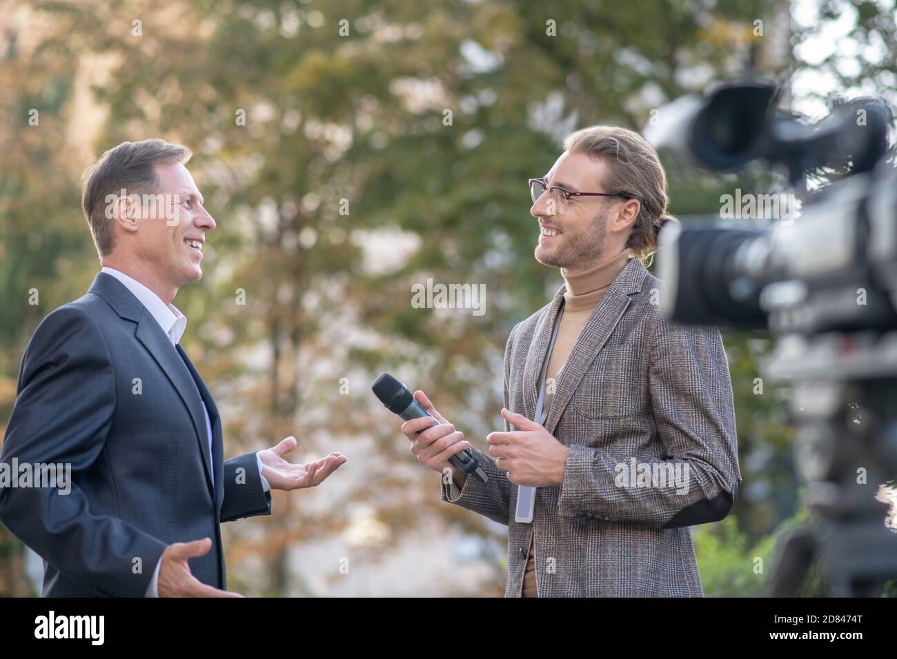 Fair-haired male journalist having interview with smiling mature male ...