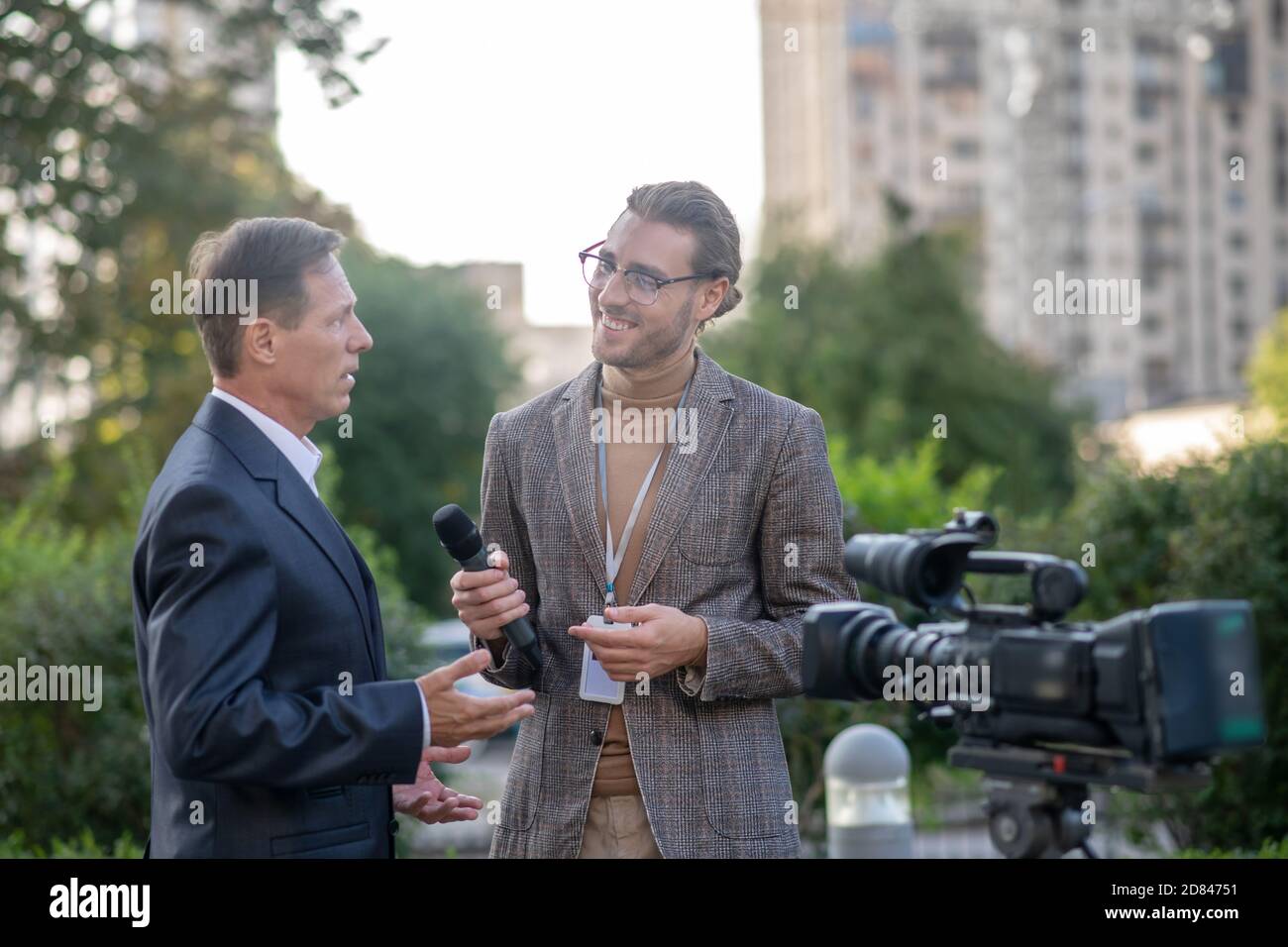 Long-haired male journalist having interview with smiling mature male ...