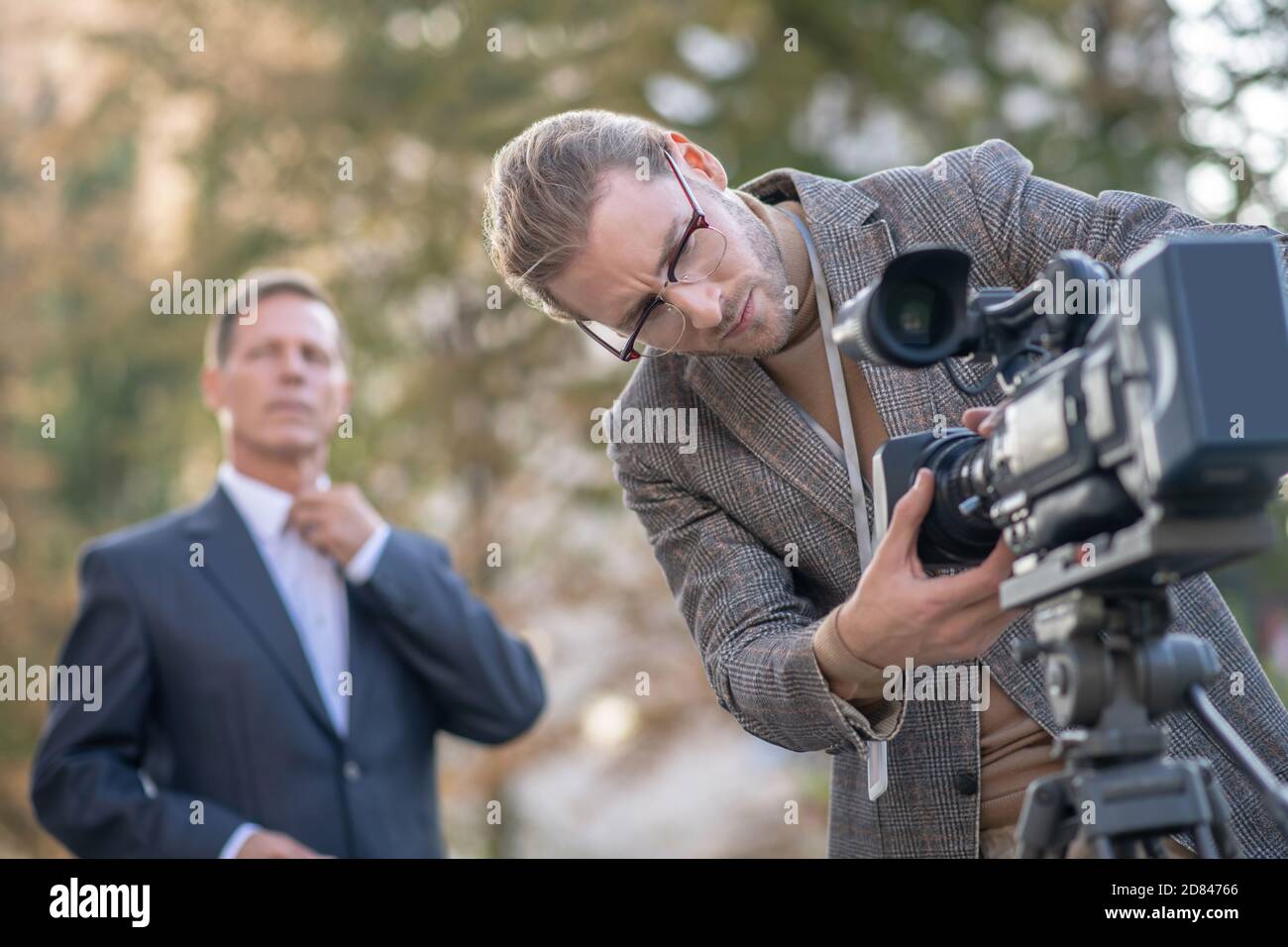 Fair-haired male journalist fitting camera to tripod before interview ...