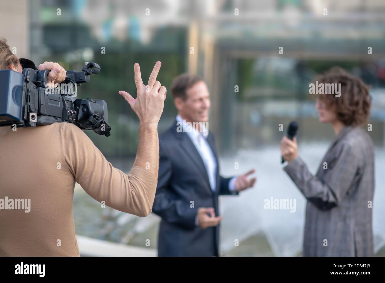 Rear view of operator filming curly female journalist interviewing ...