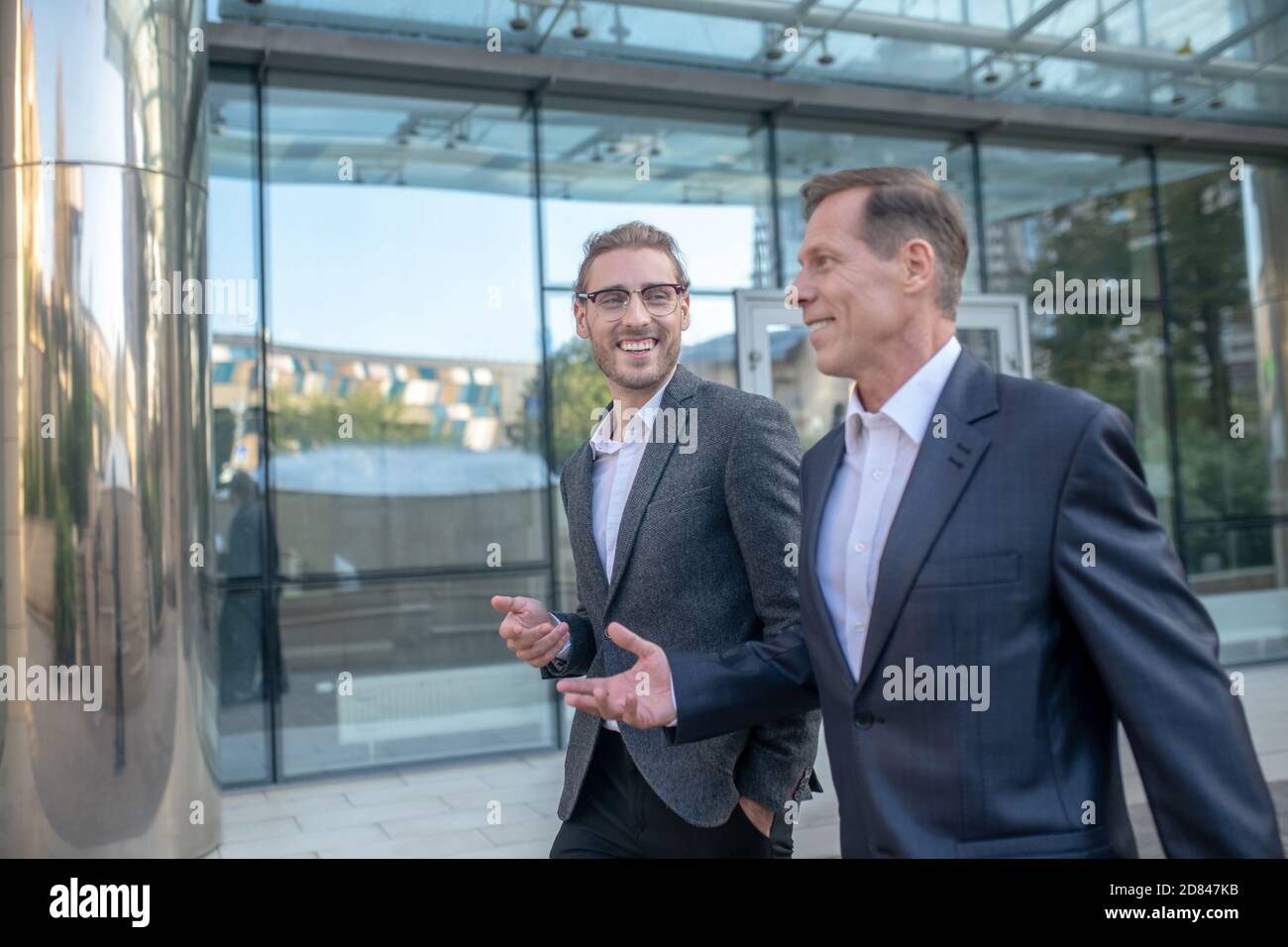 Two smiling business partners walking outside, having friendly ...