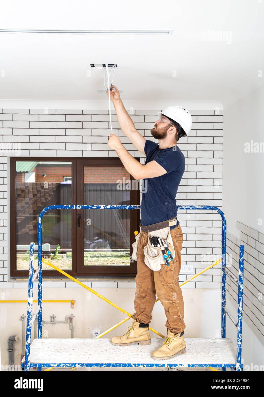 Electrician Builder at work, installation of lamps at height ...