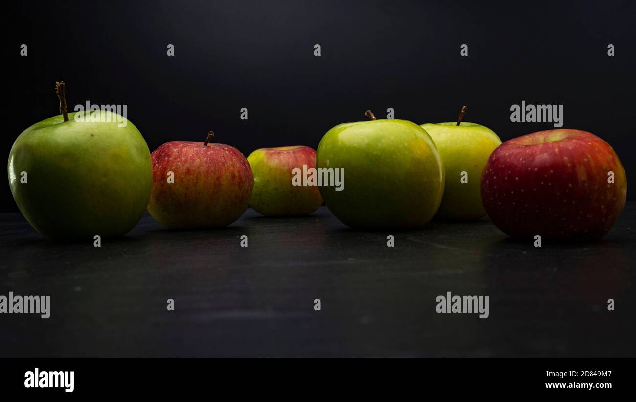 Three ripe fresh green apples and tree red apples on black table and ...
