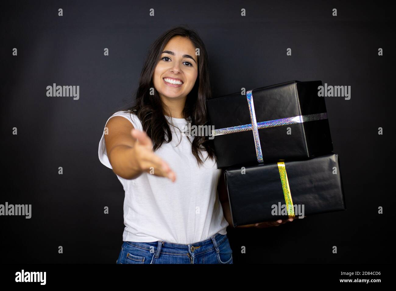 Young beautiful woman holding gifts over isolated black background ...