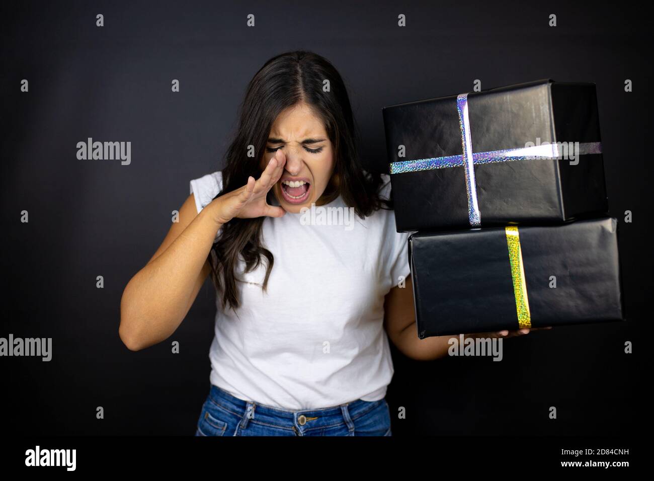 Young beautiful woman holding gifts over isolated black background ...