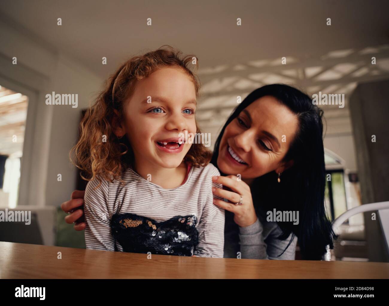Happy Mother Playing With Daughter At Home While Sitting On Chair At
