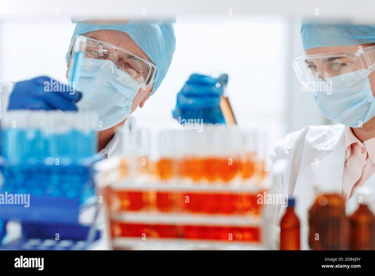 scientists in protective masks standing in front of a rack of test ...