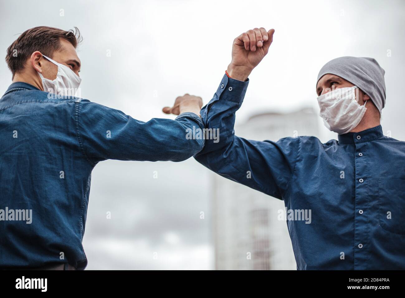 two friends greeting each other with their elbows on a city street ...