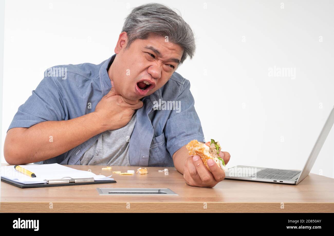 Asian man working and eating a burger on office desk and holding his ...
