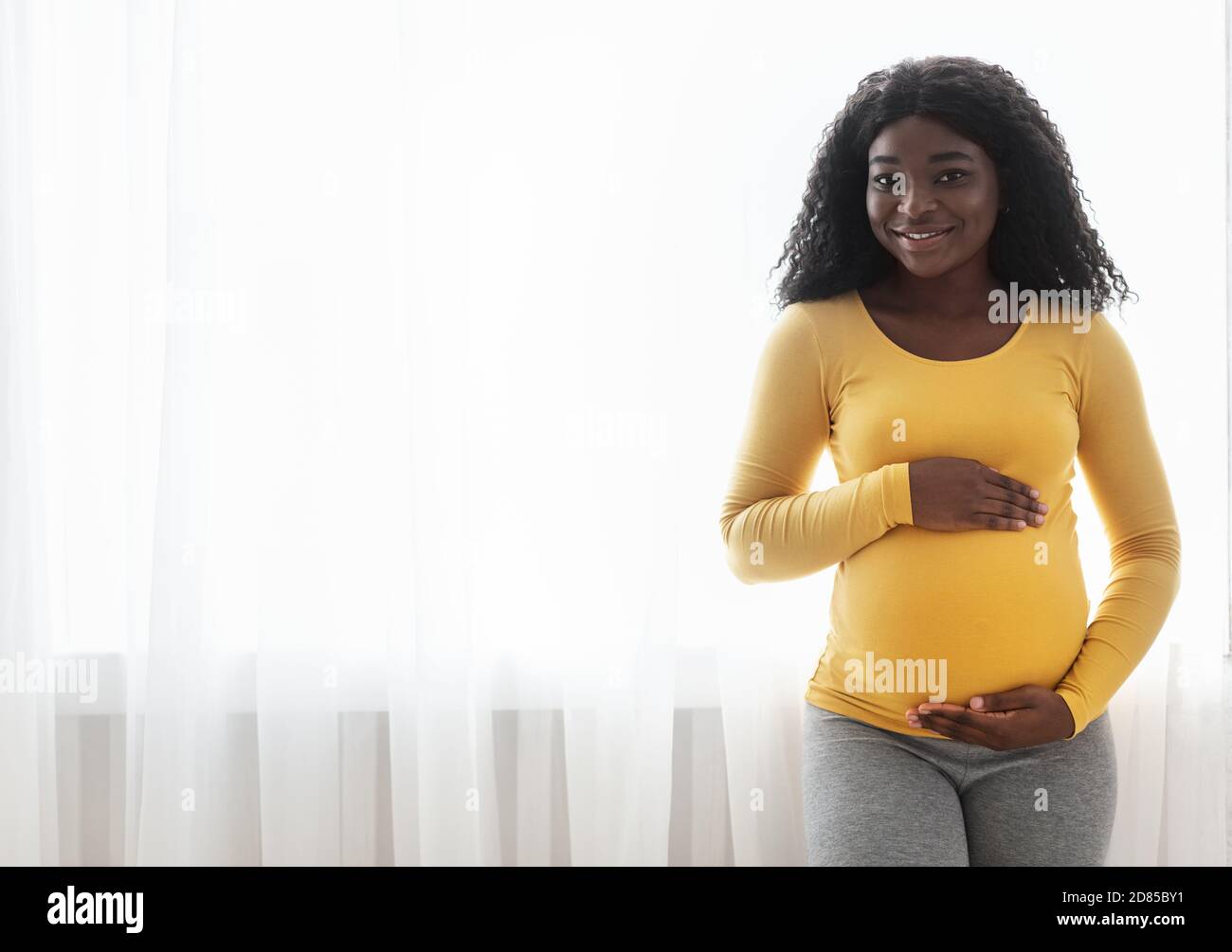 Smiling black lady carrying baby, hugging her big tummy Stock Photo - Alamy