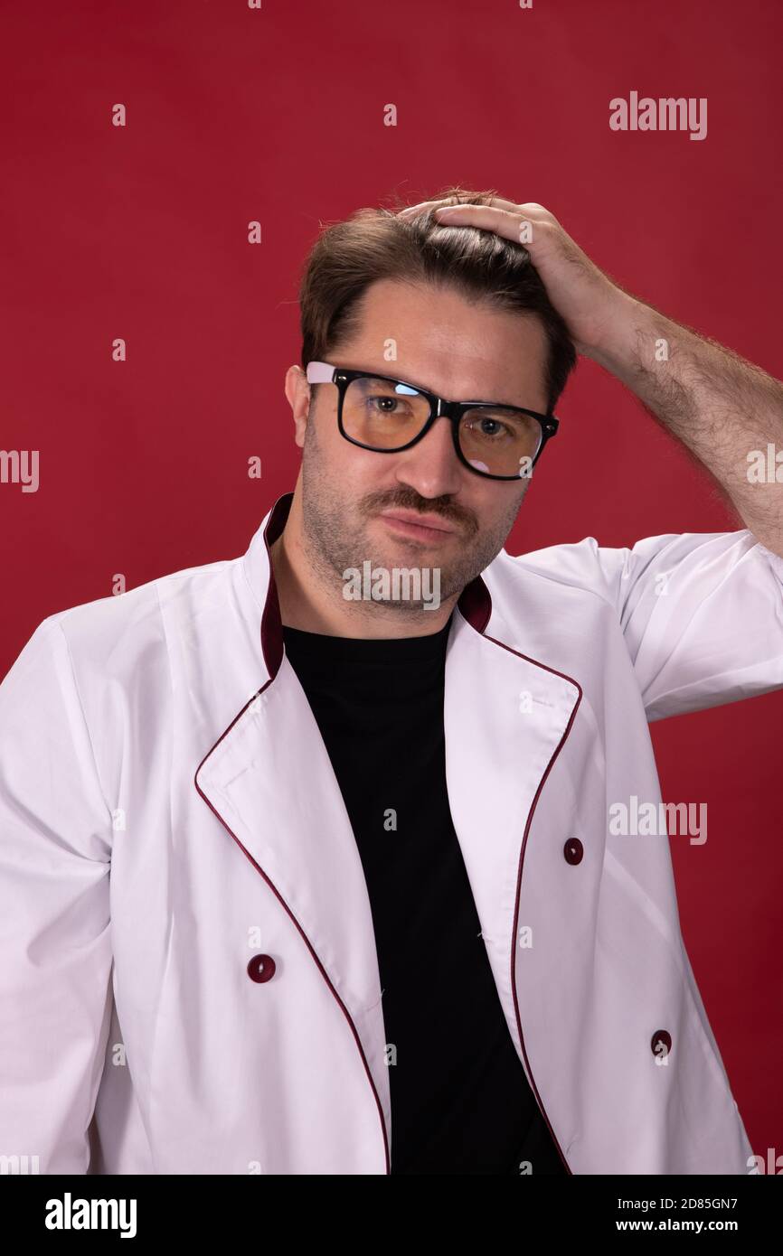 Unshaven male cook in uniform without headdress touches his head ...