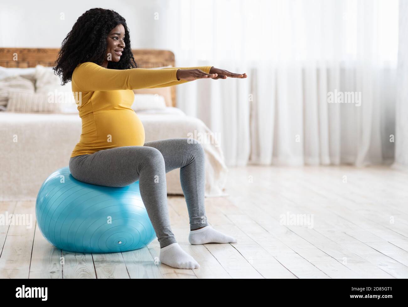 Black expecting woman training on ball, getting ready for childbirth ...