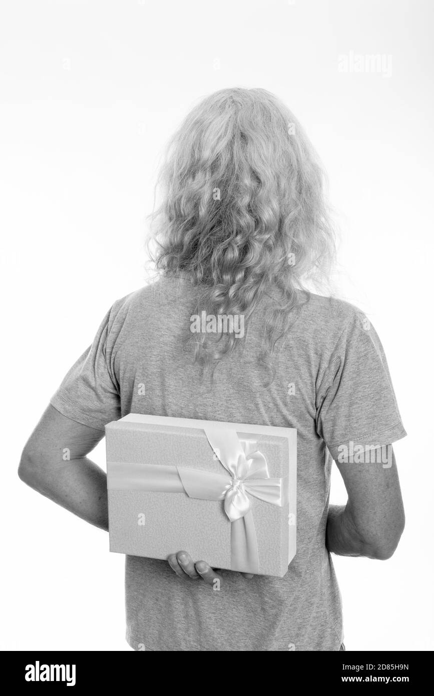Back view of senior bearded man hiding gift box behind back ready for ...