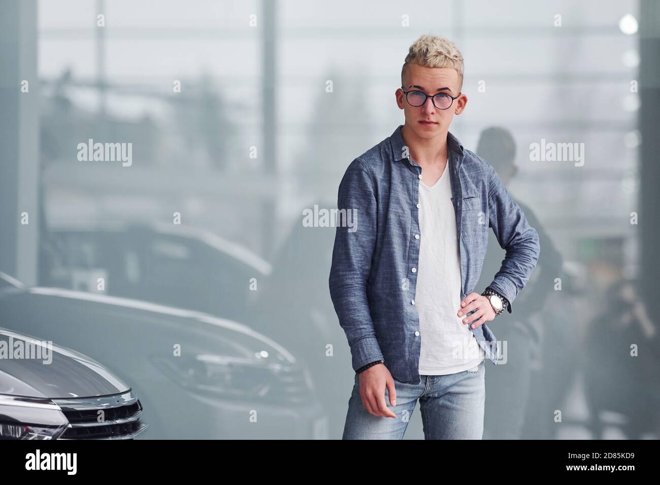 Young hipster guy in nice clothes stands indoors against grey ...