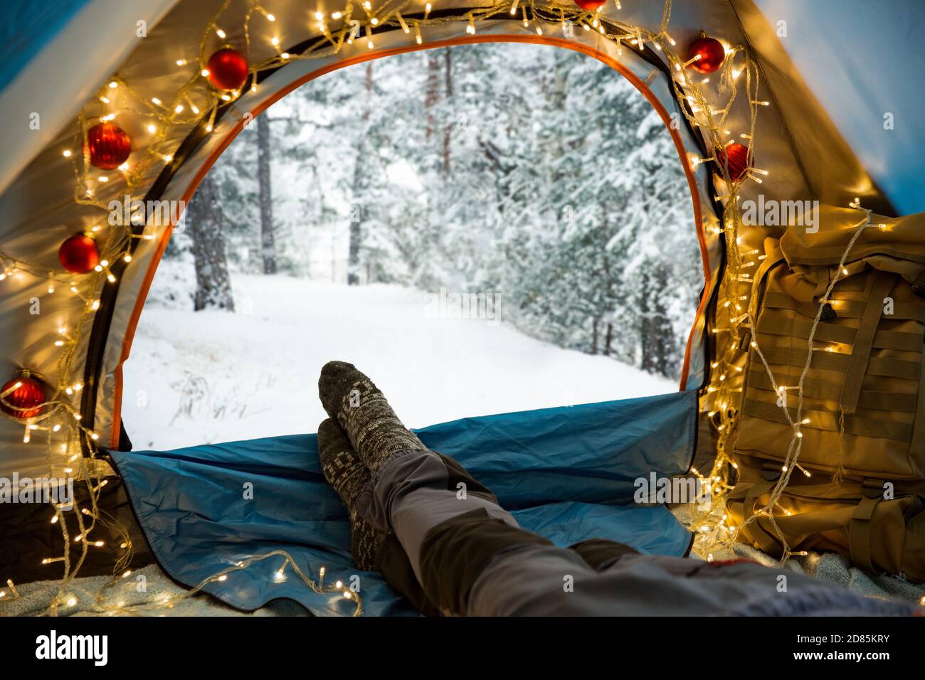 A man lying in a tent decorated with Christmas lights wearing warm ...