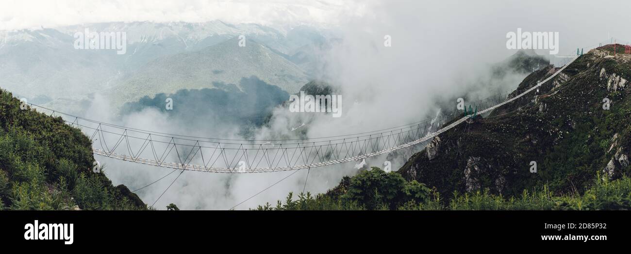 Wide angle view of a long suspension bridge hangs over an abyss between ...