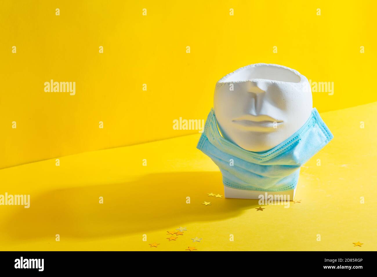 Gypsum craft pot in the shape of human face with protective medical mask under his chin on a ...