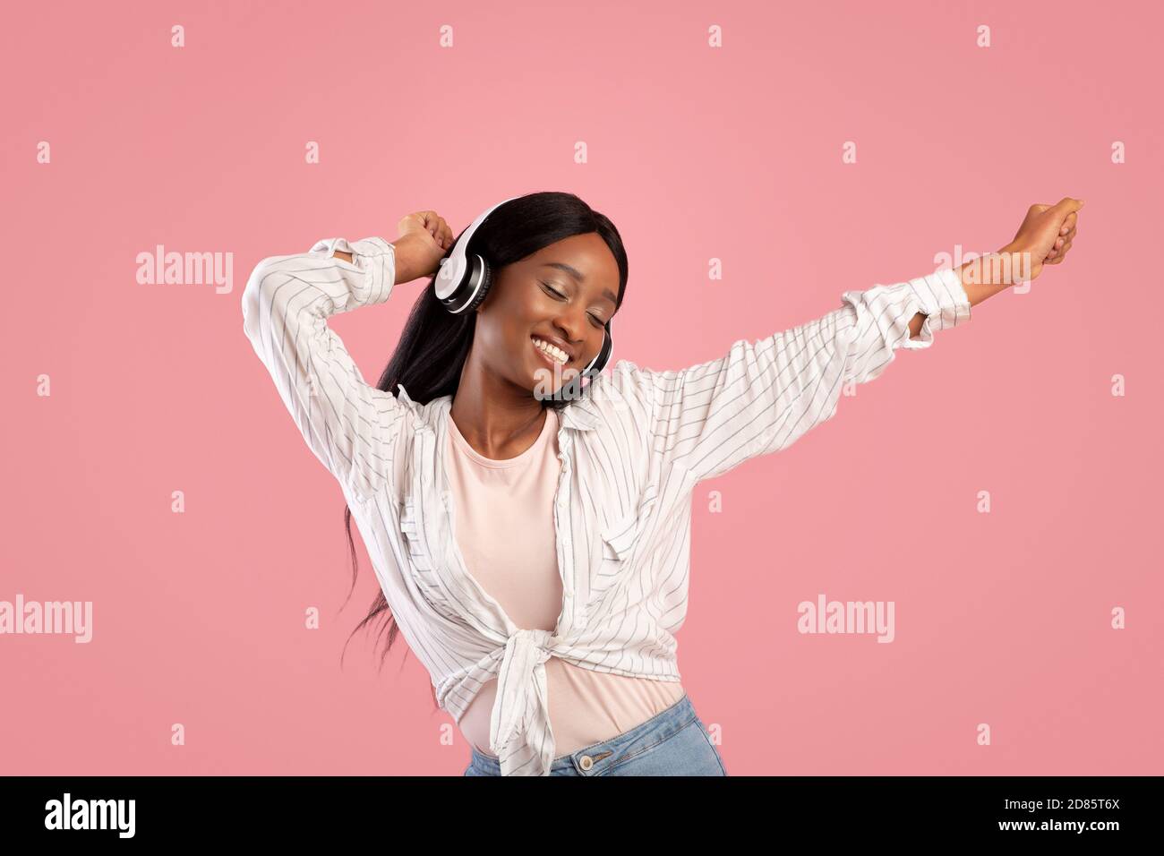 Happy black woman in headset dancing to beautiful music on pink studio ...