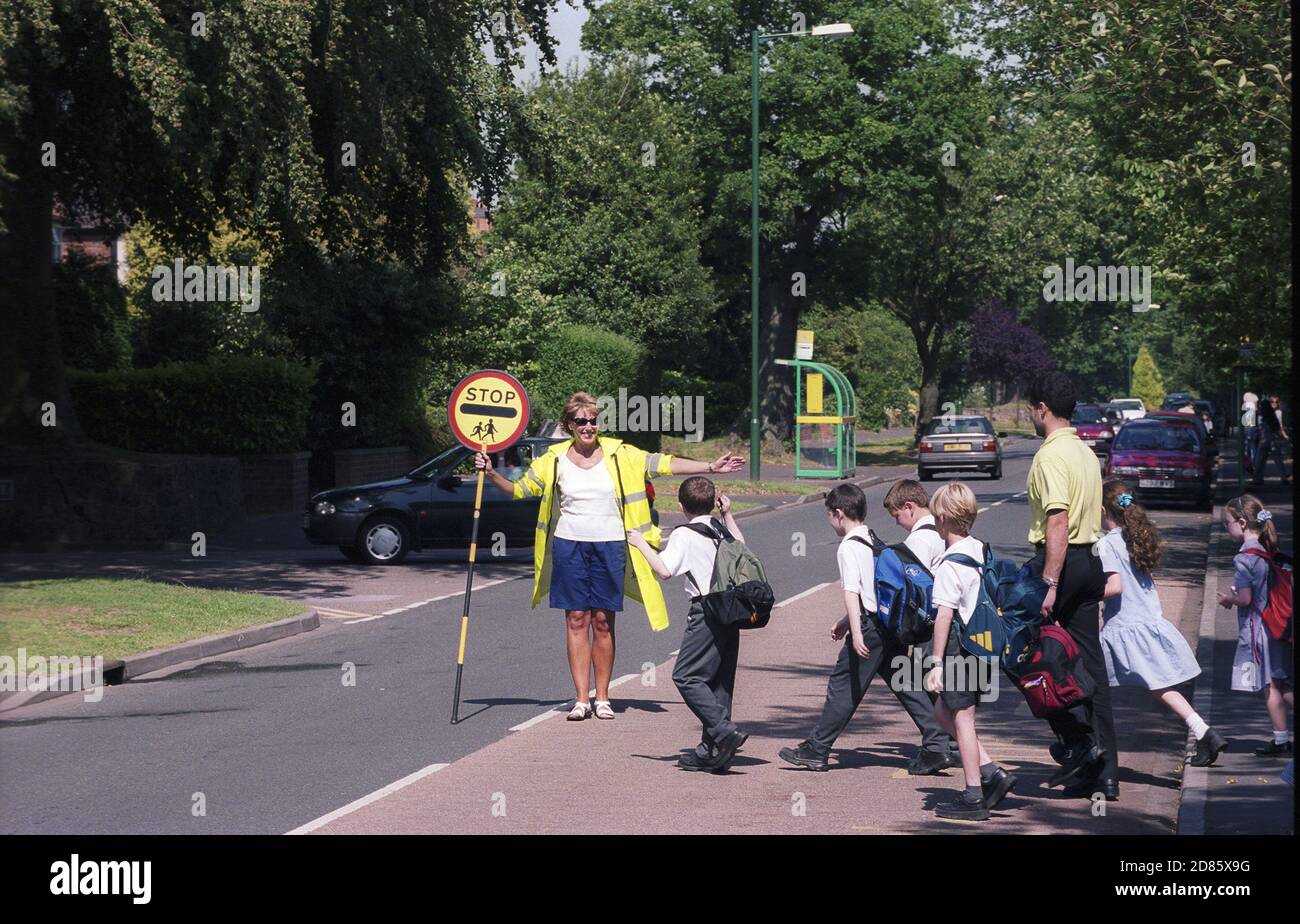 A lollipop lady guides school children across the road in Solihull ...