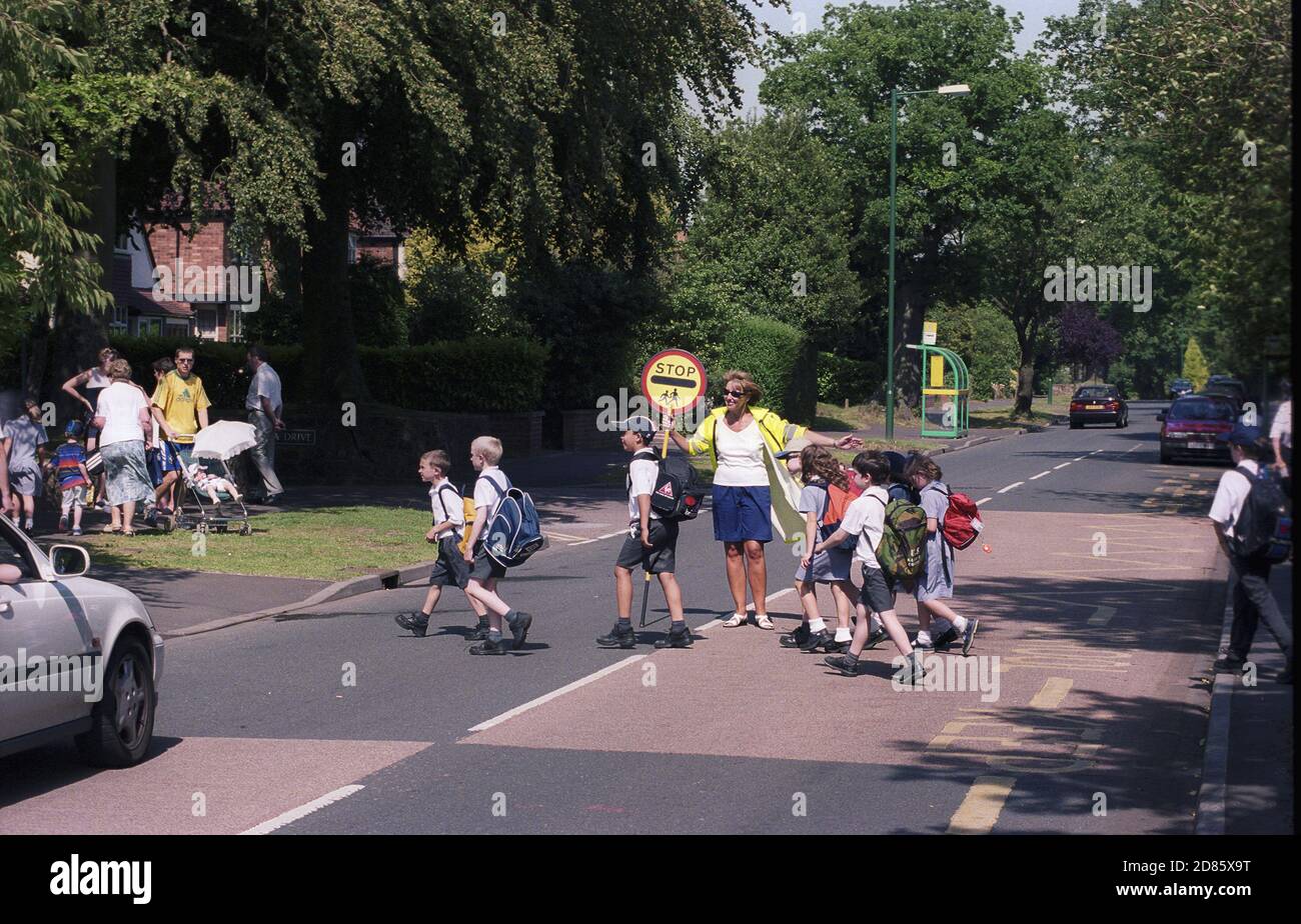 A lollipop lady guides school children across the road in Solihull ...