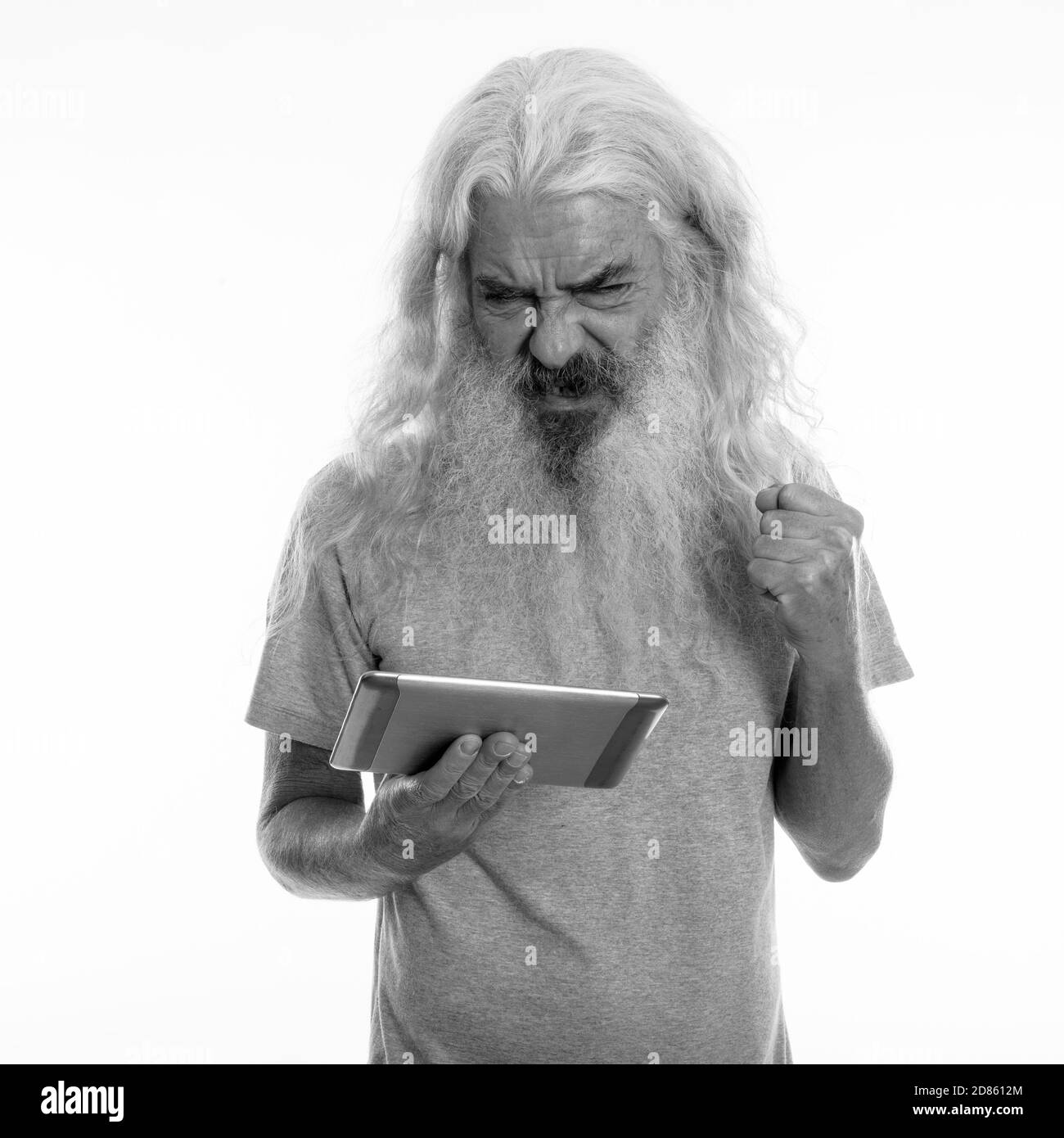 Studio shot of senior bearded man using digital tablet while looking ...