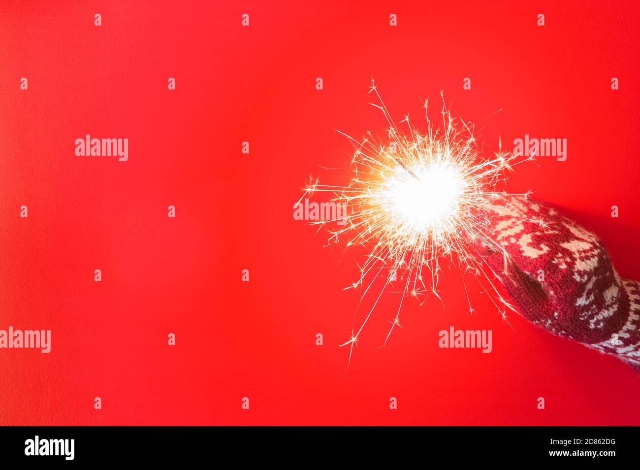 Hand in mitten holding burning sparkler on red background. Bengal fire ...