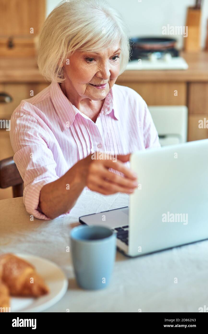 Smiling elderly female using laptop while looking at screen at the ...