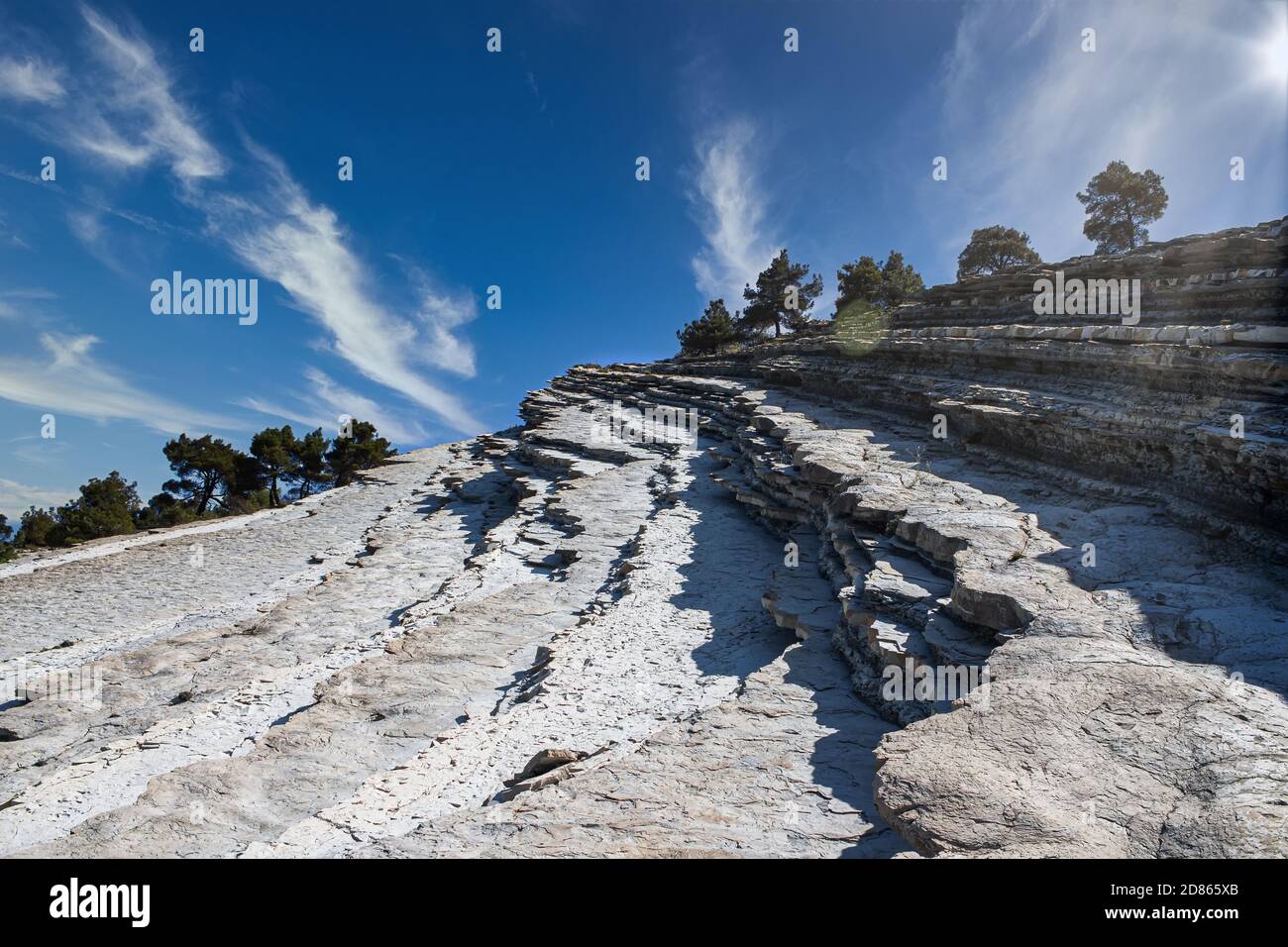 The top of the cliff with trees against the bright blue sky with clouds ...
