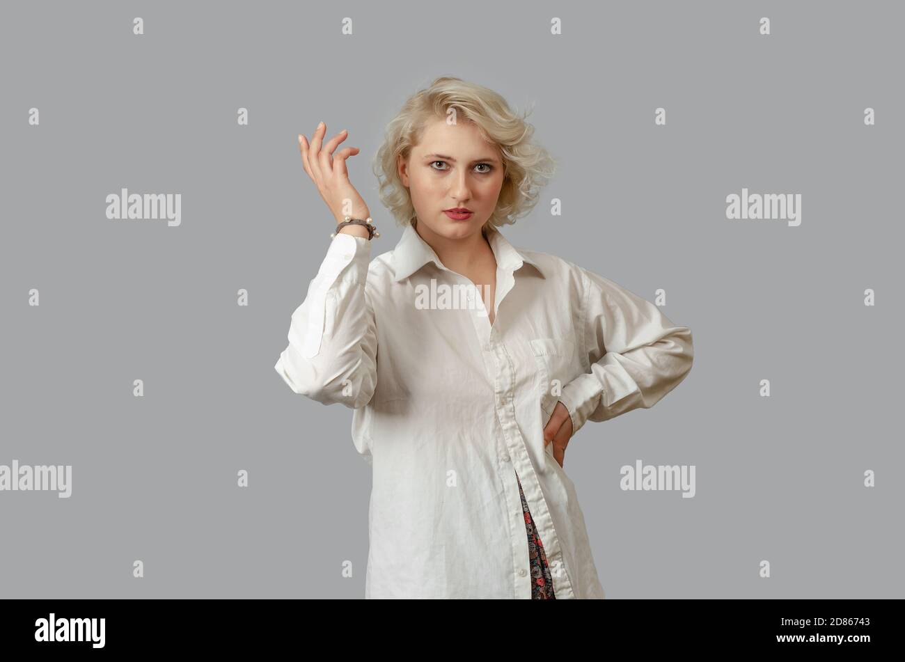 Young blonde woman in a white shirt looks at camera, hand on hand ...