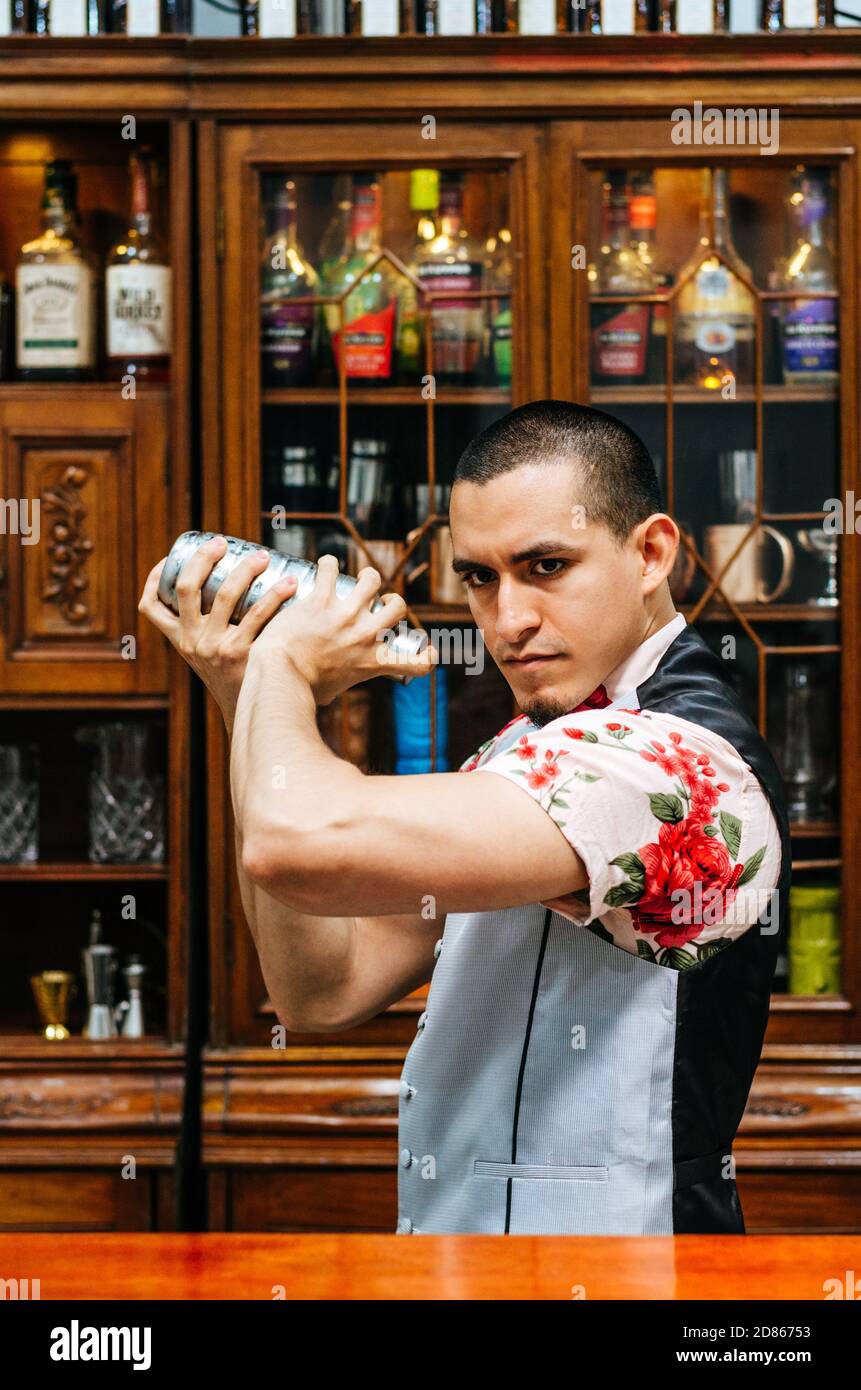 Young handsome smiling barman in bar interior shaking and mixing ...