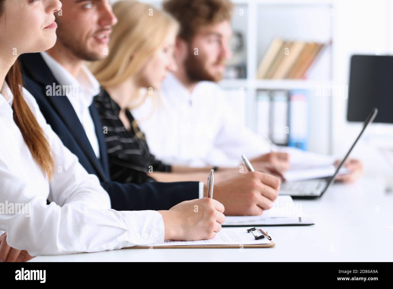 A group of people at a seminar make notes in a notebook with a pen ...