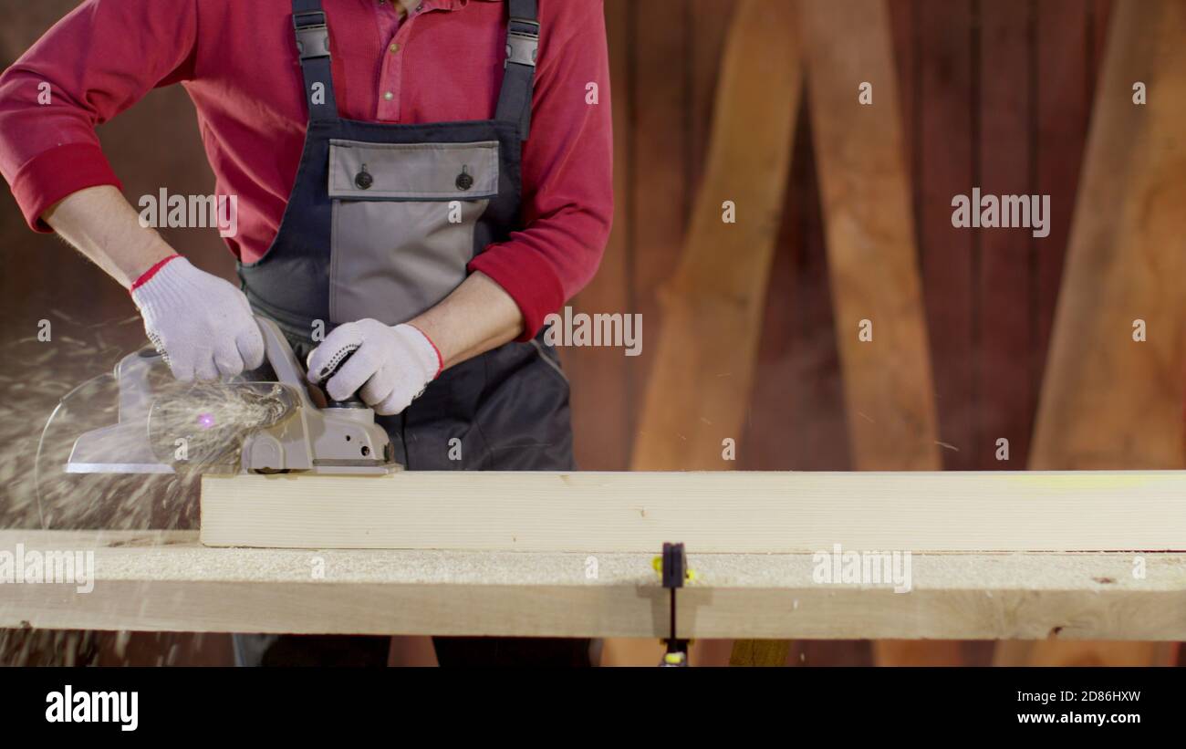 Close-up hands of carpenter in overalls polish surface of blank with ...