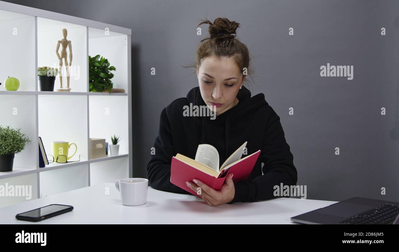 Caucasian girl in black hoody reading book yawning and falling asleep ...
