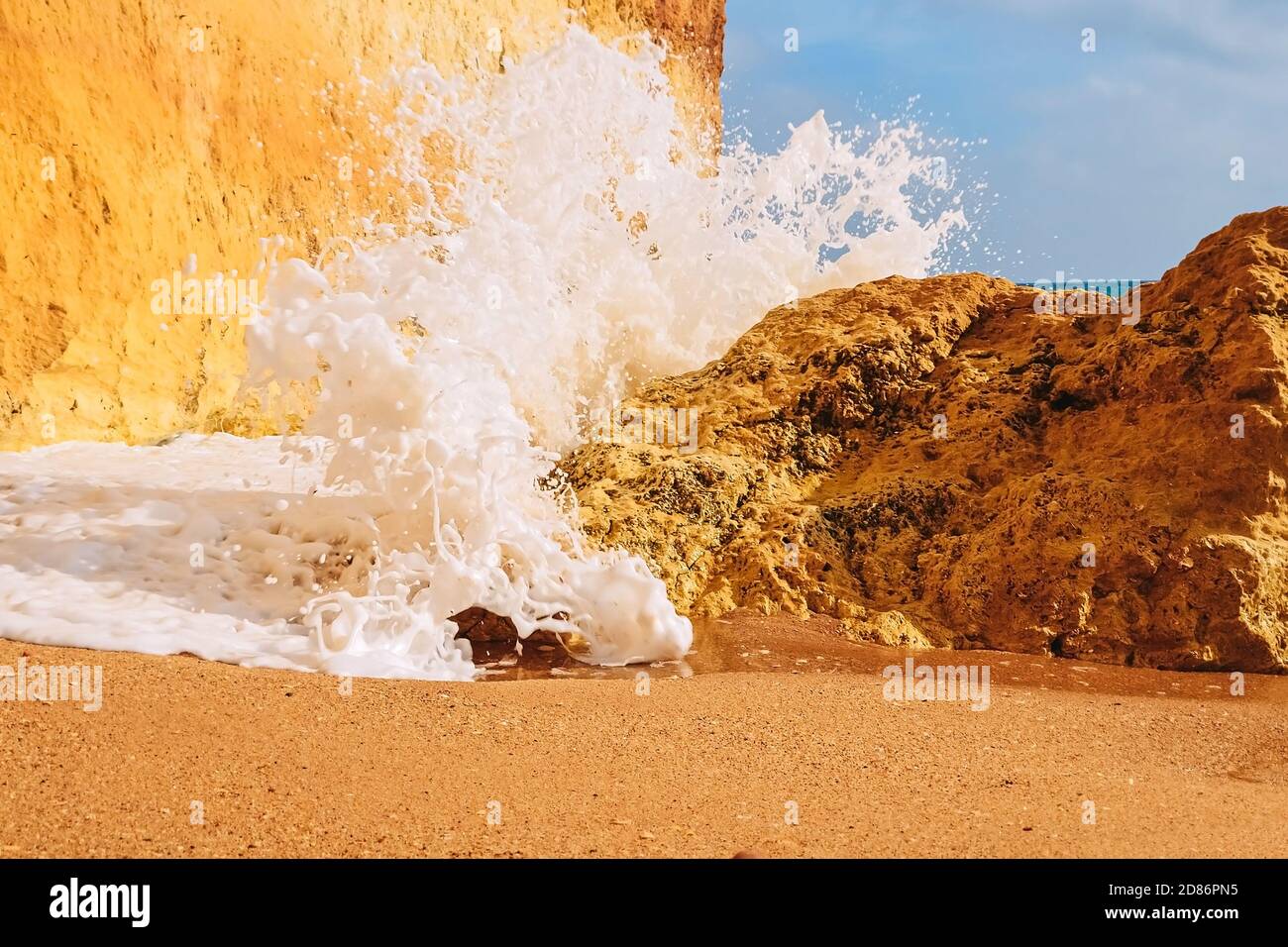 Waves crash on rocks on the sandy shores of benagil beach in portugal ...